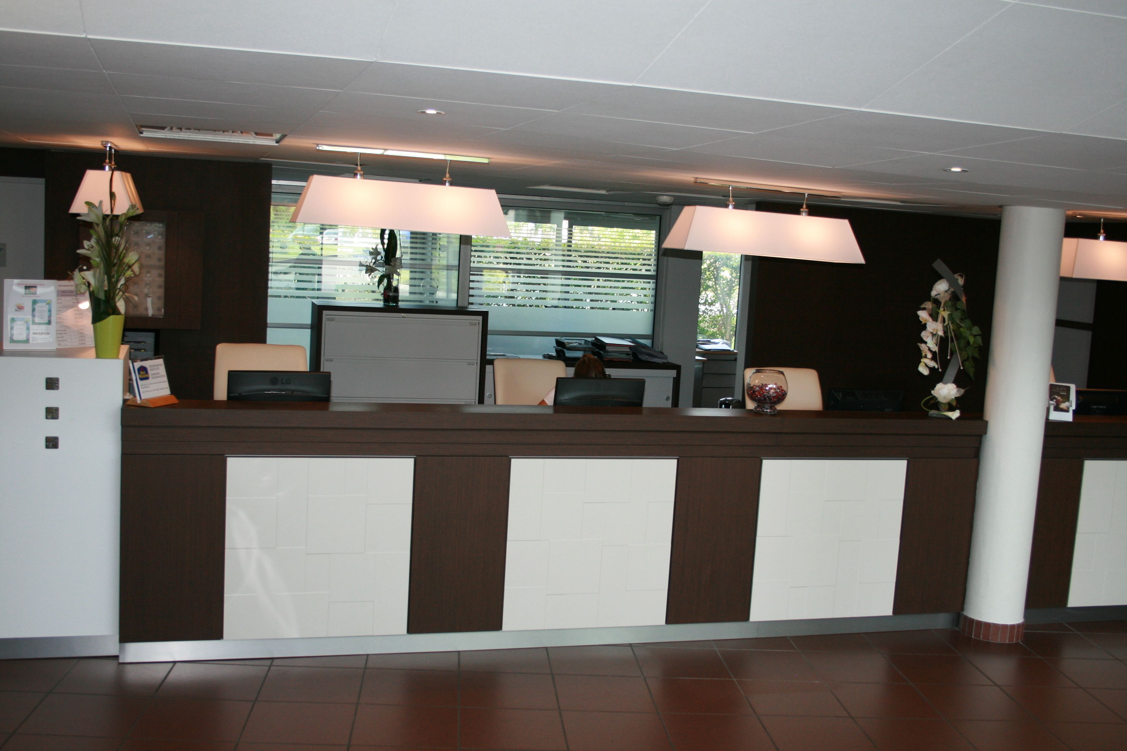 Uma receção com design moderno, apresentando uma combinação de painéis de madeira escura e clara, uma janela grande com persianas e duas luzes pendentes.