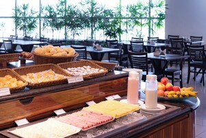 Buffet com diversos alimentos e vista para a área de refeições, com mesas e cadeiras.