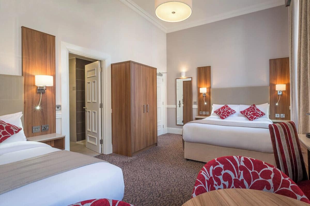Quarto de hotel com duas camas, área de estar com uma mesa e um guarda-roupa.