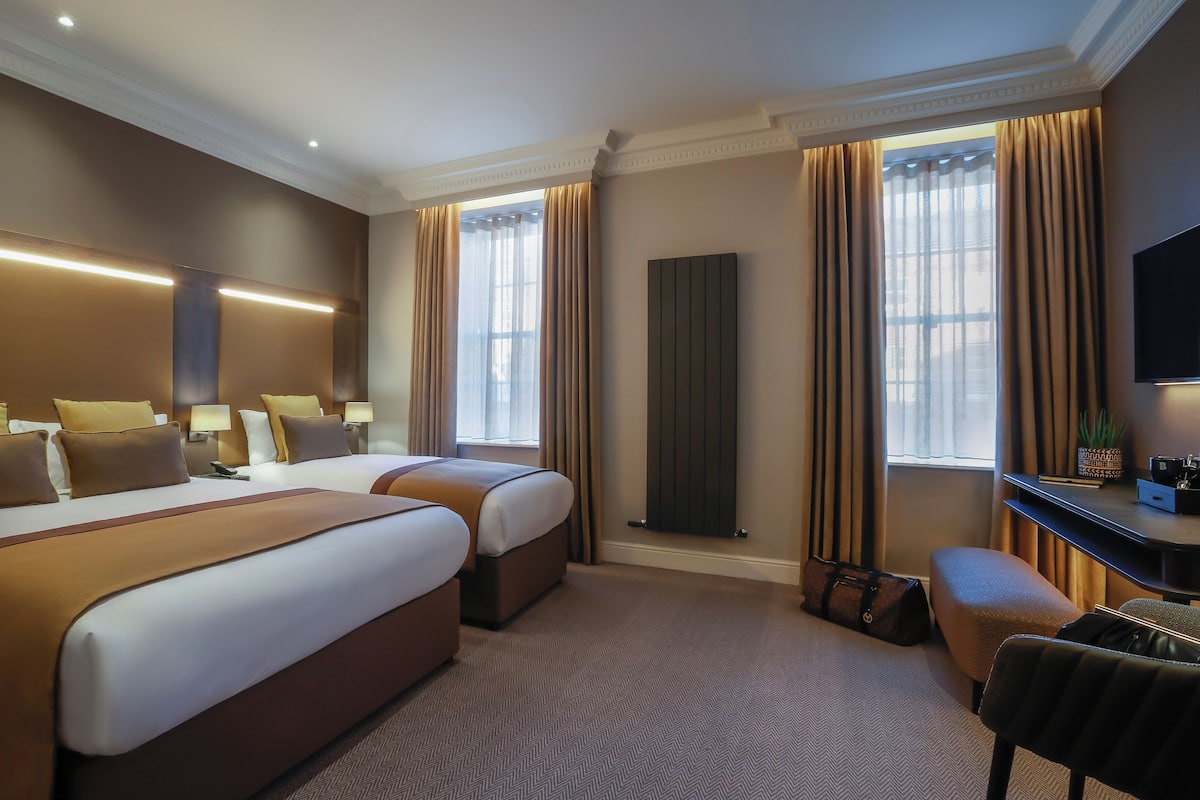 Quarto de hotel com duas camas, uma escrivaninha, uma cadeira e uma televisão.