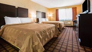 Quarto de hotel com duas camas, uma televisão e uma escrivaninha.