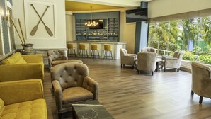 Um hall amplo com área de bar, assentos confortáveis e uma grande janela com vista para o verde.