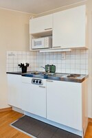 Cozinha compacta com armários brancos, micro-ondas e fogão.