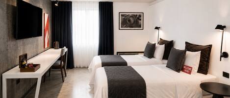 Quarto de hotel com duas camas, uma escrivaninha, televisão de tela plana e janela com cortinas.