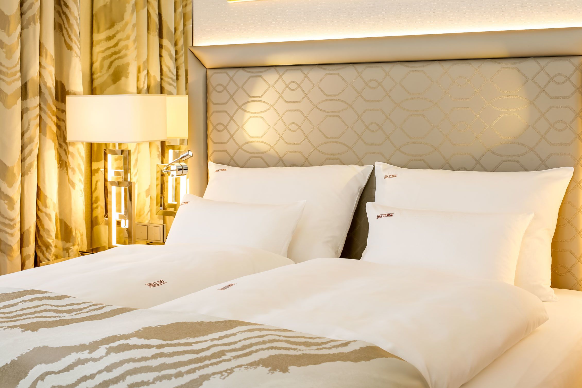 Quarto de hotel com uma cama grande, duas mesas de cabeceira, uma luminária e uma cabeceira estampada.