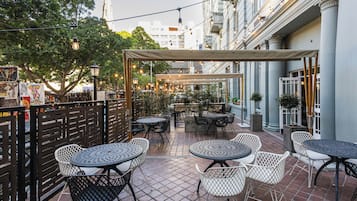 Uma área de estar ao ar livre com mesas, cadeiras, uma pérgola e luzes de cordão.