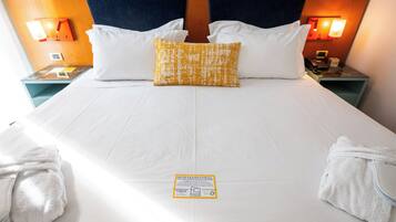 Quarto de hotel com cama, duas almofadas, mesa de cabeceira, luminária e toalha.