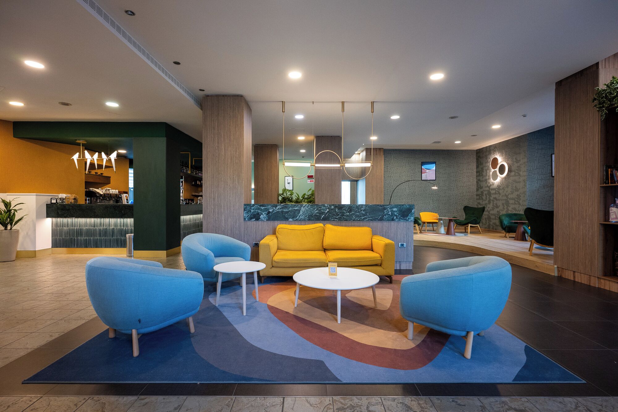 Um hall moderno com balcão de recepção, área de estar com sofás e cadeiras, e um bar.