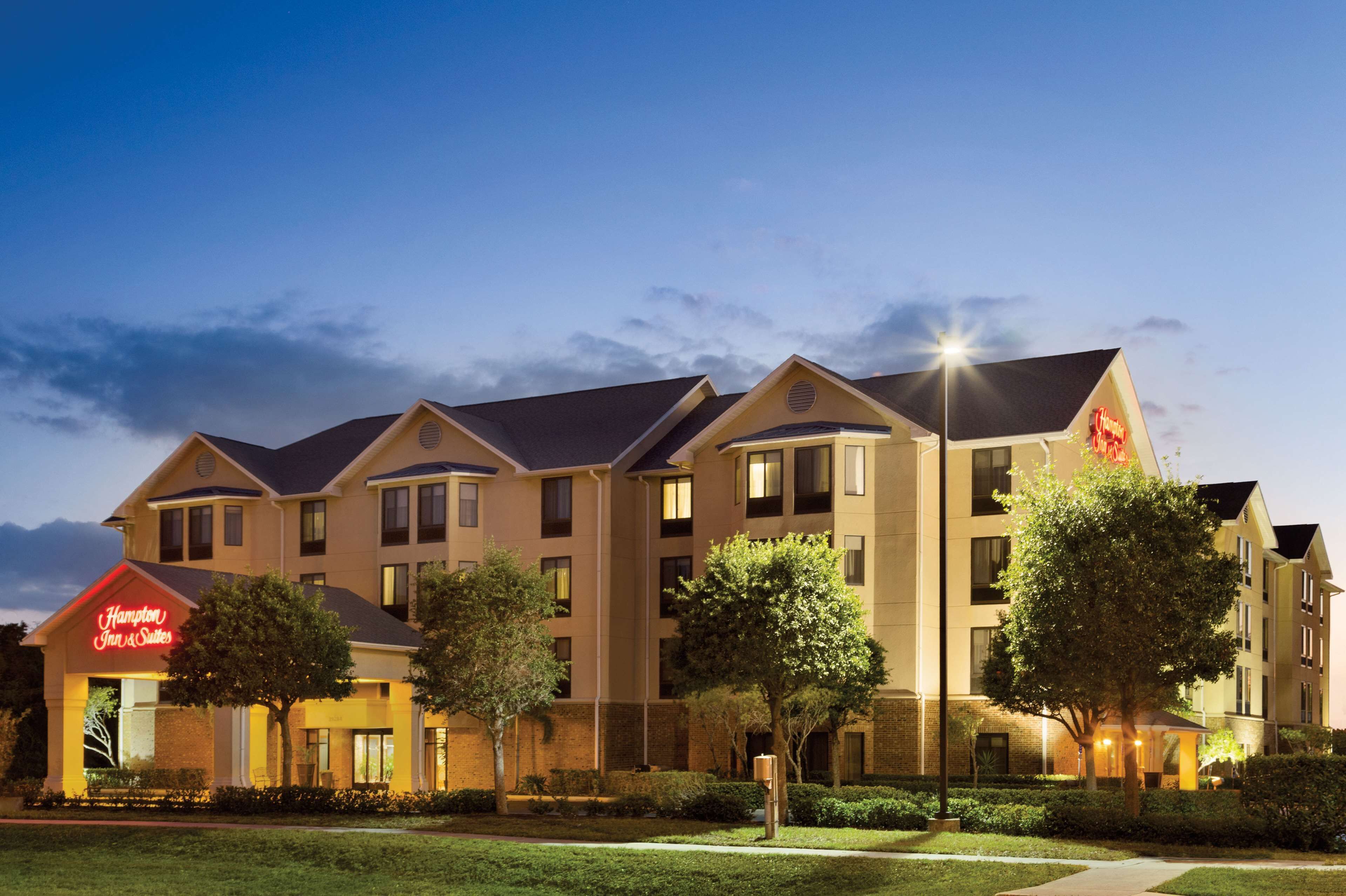 Um hotel Hampton Inn & Suites com design moderno, apresentando vários andares e fachada bem iluminada.