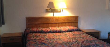 Quarto de hotel com cabeceira de madeira, colcha estampada, duas mesas de cabeceira e luminária fixada na parede.