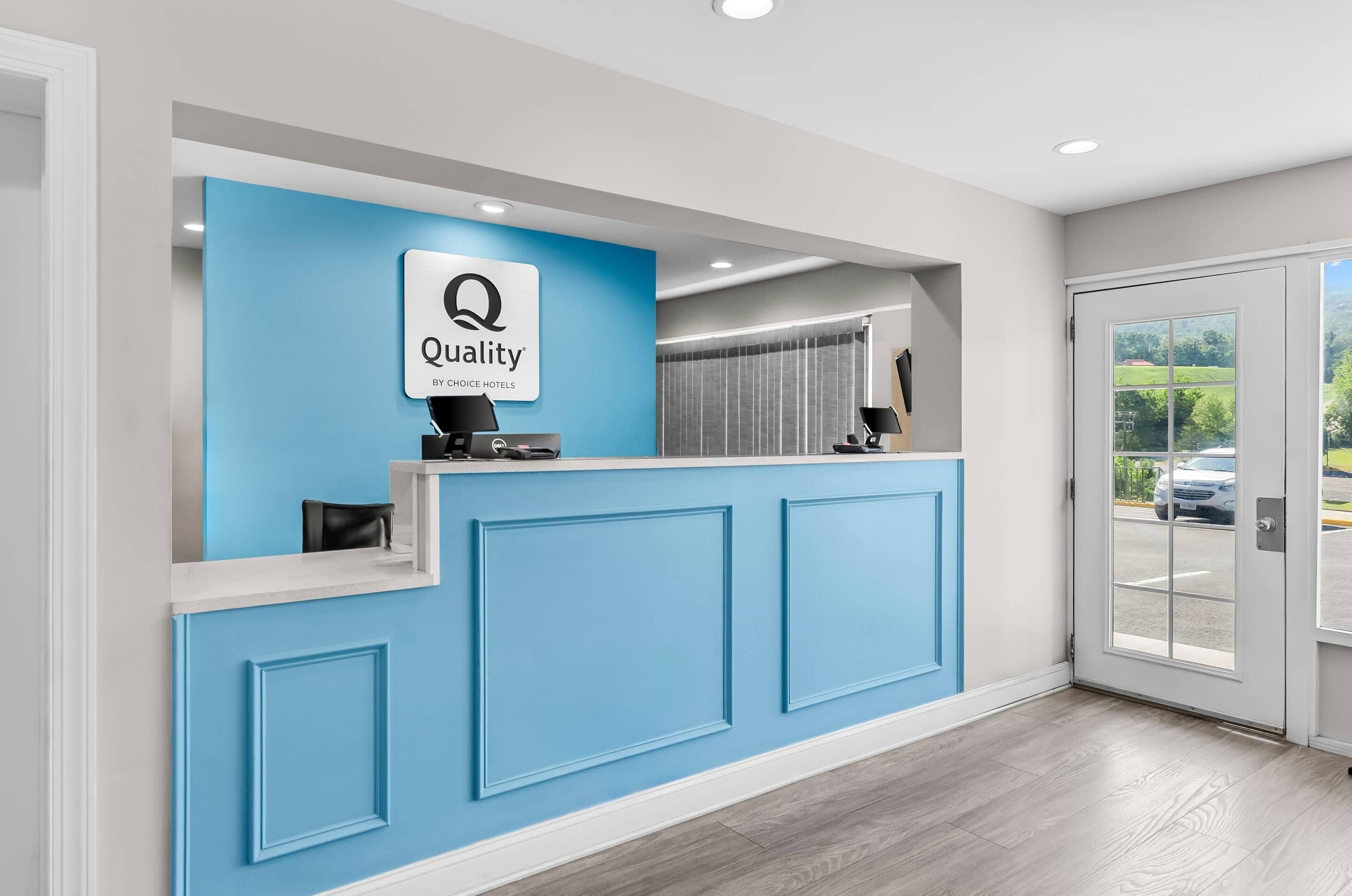 Uma mesa de recepção com uma parede azul de destaque e uma placa com a inscrição 'Quality by Choice Hotels'.