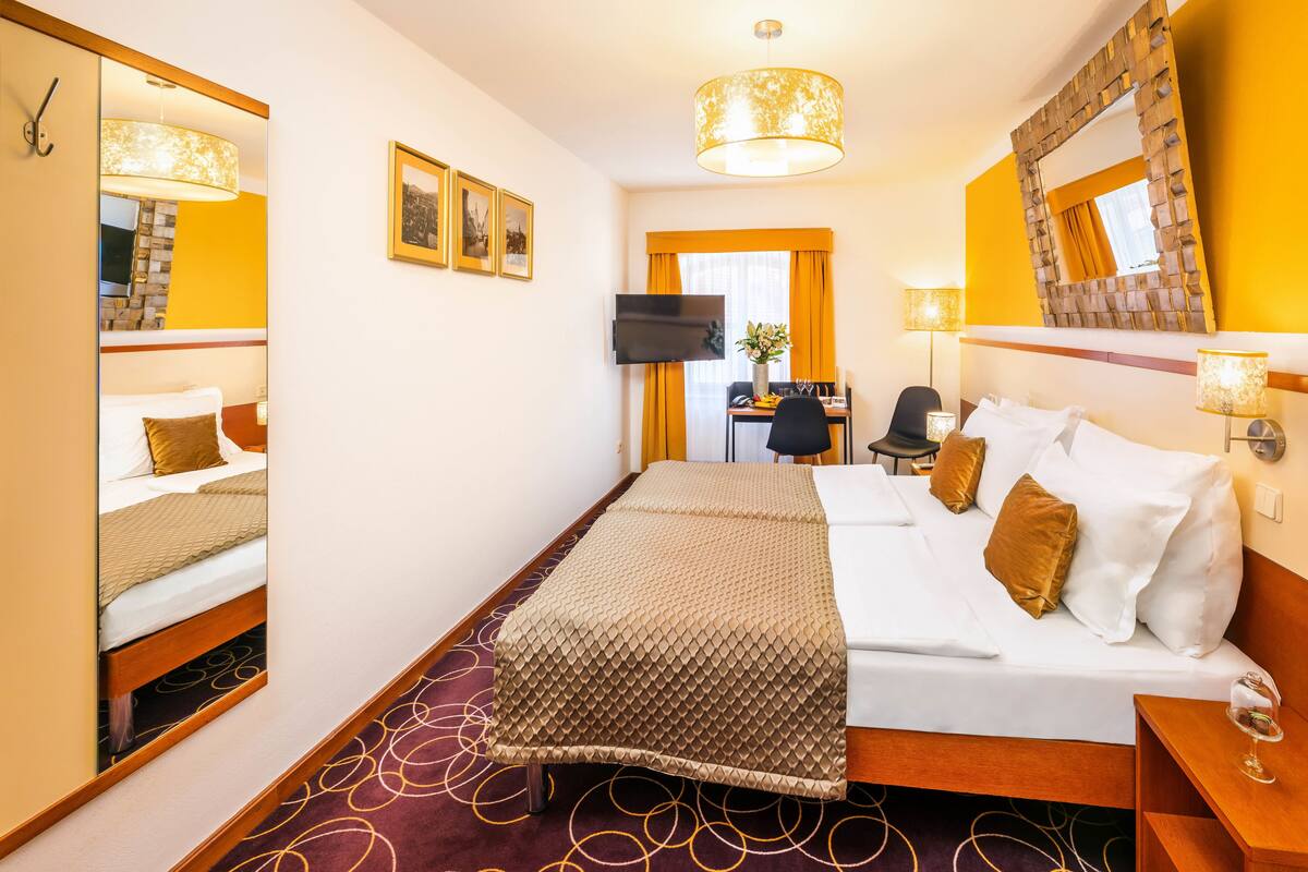 Quarto de hotel com cama, escrivaninha, cadeira, televisão e espelho.