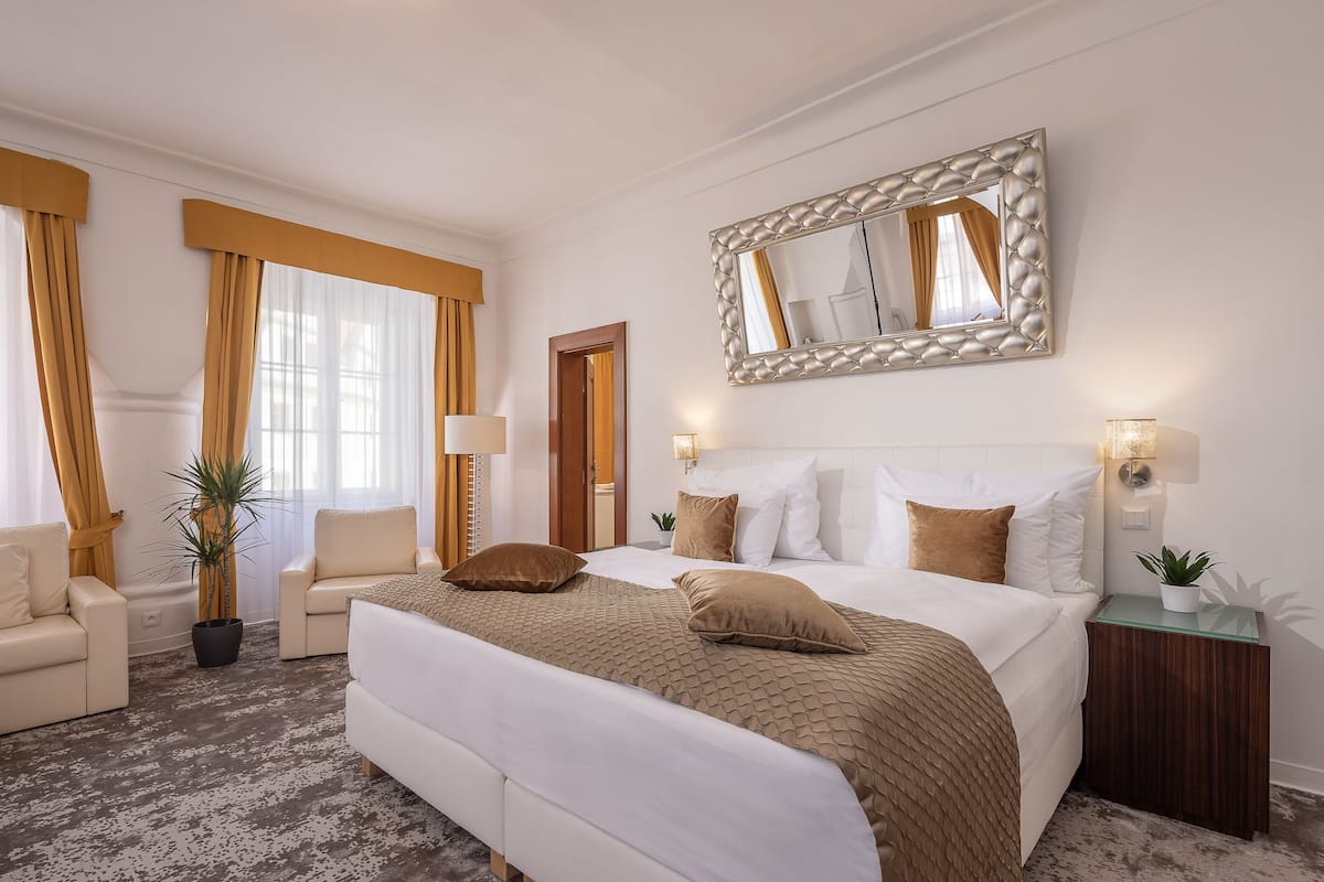 Quarto de hotel com uma cama grande, duas mesas de cabeceira, um espelho e um vaso de planta.