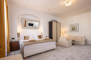 Quarto de hotel com uma cama grande, mesa de cabeceira, espelho, guarda-roupa, sofá e abajur.