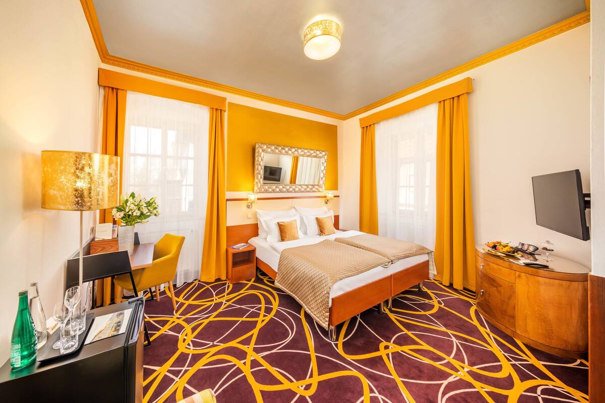 Quarto de hotel com cama, escrivaninha, cadeira, televisão e banheiro.