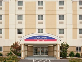 Entrada de um hotel com uma placa indicando 'CANDLEWOOD SUITES' e um estacionamento em frente.