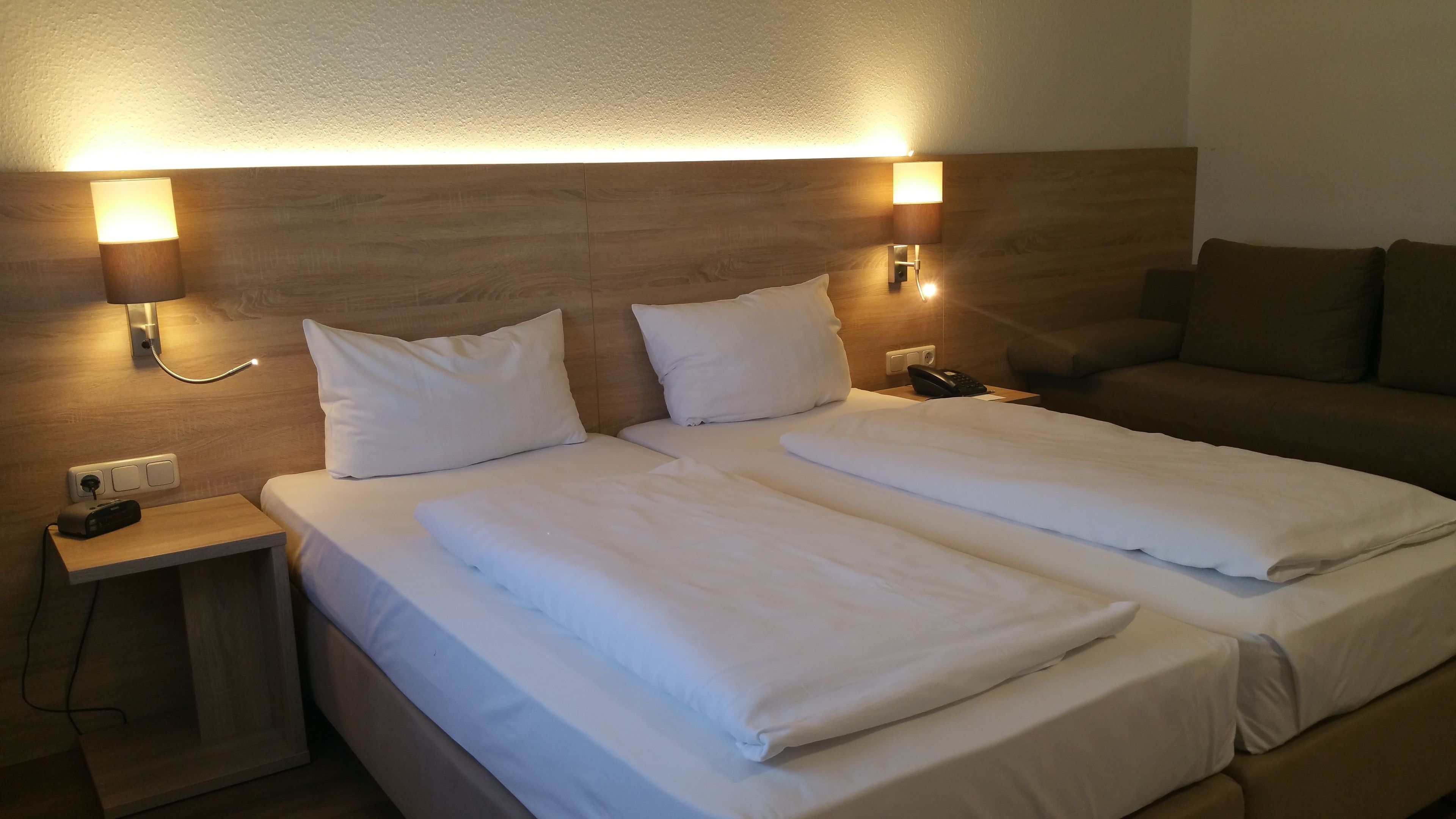 Quarto de hotel com duas camas, uma mesinha de cabeceira com telefone e um sofá.