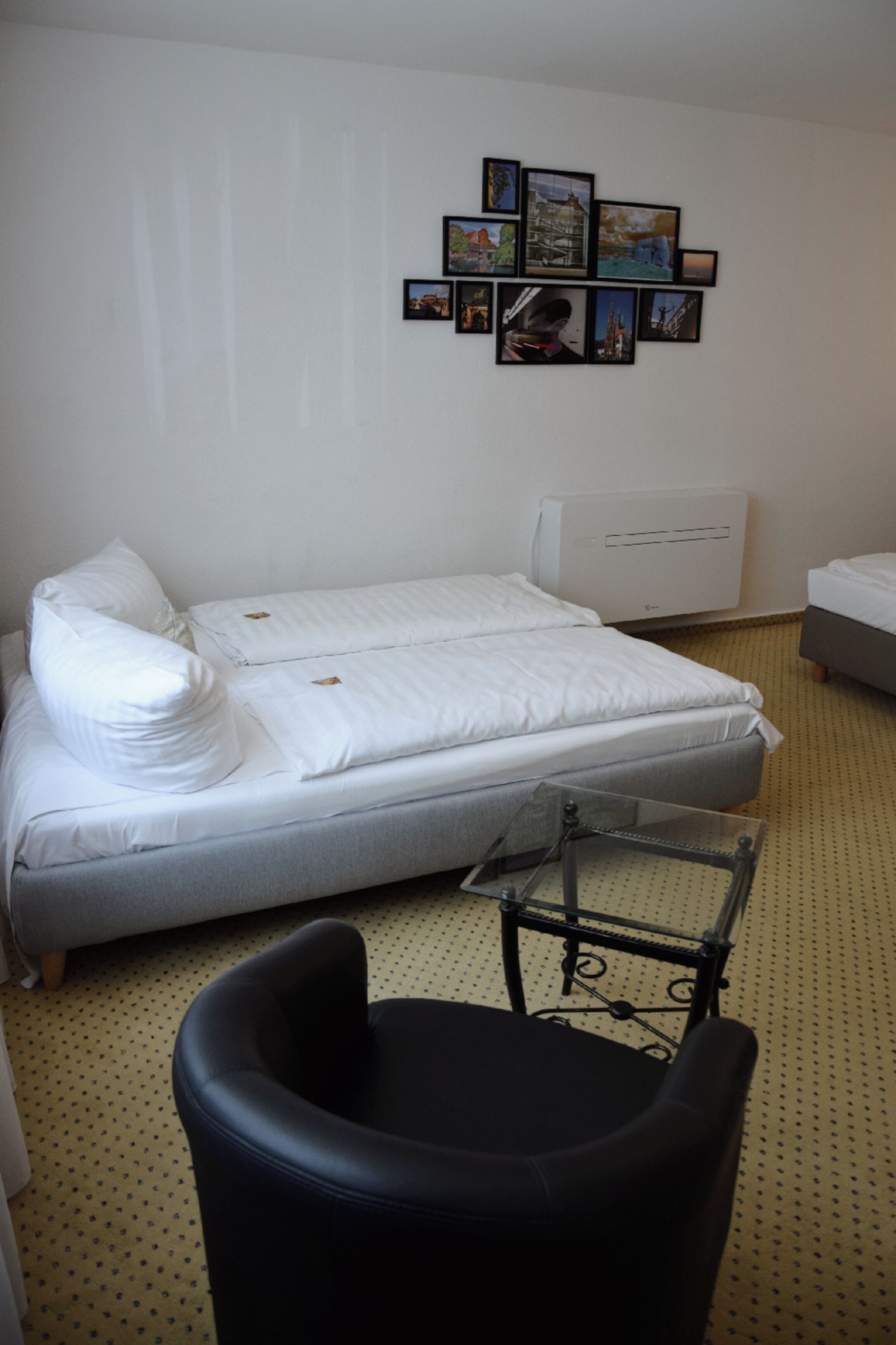 Quarto de hotel com uma cama, uma cadeira e uma parede com quadros.