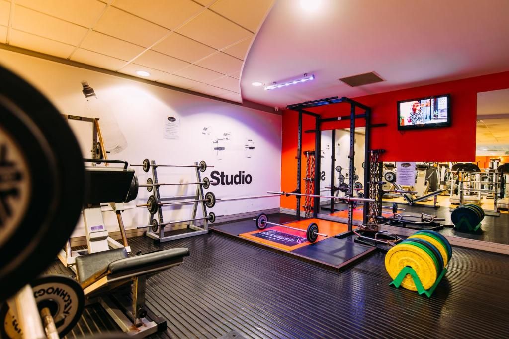 Uma academia com equipamentos de musculação, uma televisão e uma parede vermelha de destaque.