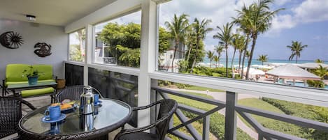 Uma varanda com móveis de vime, uma mesa de vidro e vista para um resort à beira-mar.