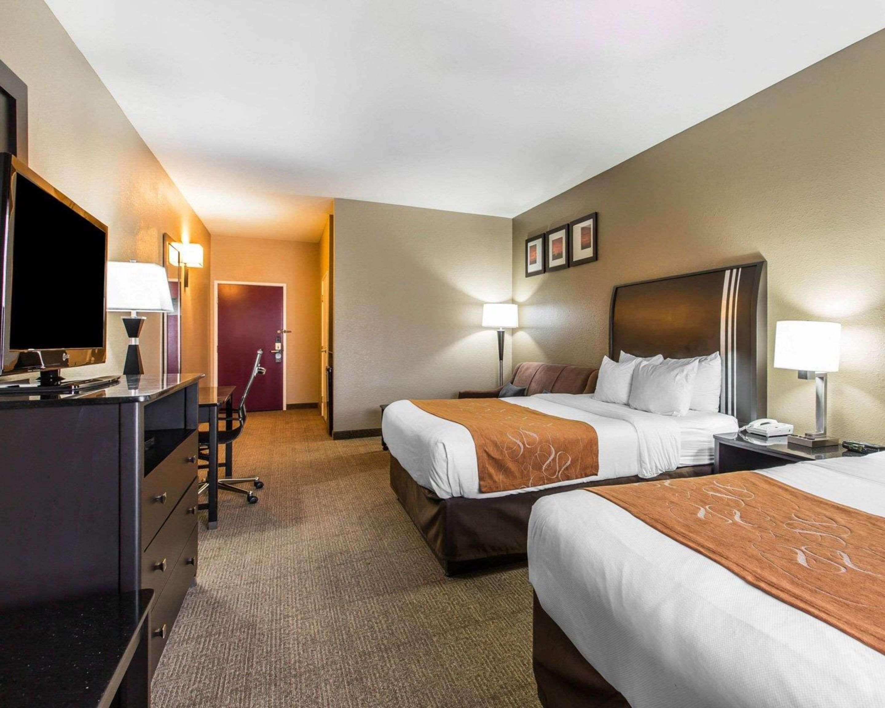 Quarto de hotel com duas camas, uma escrivaninha, uma cadeira, uma televisão e uma porta.