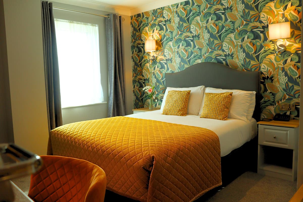 Quarto de hotel com cama, mesa de cabeceira, cadeira e janela com cortinas.