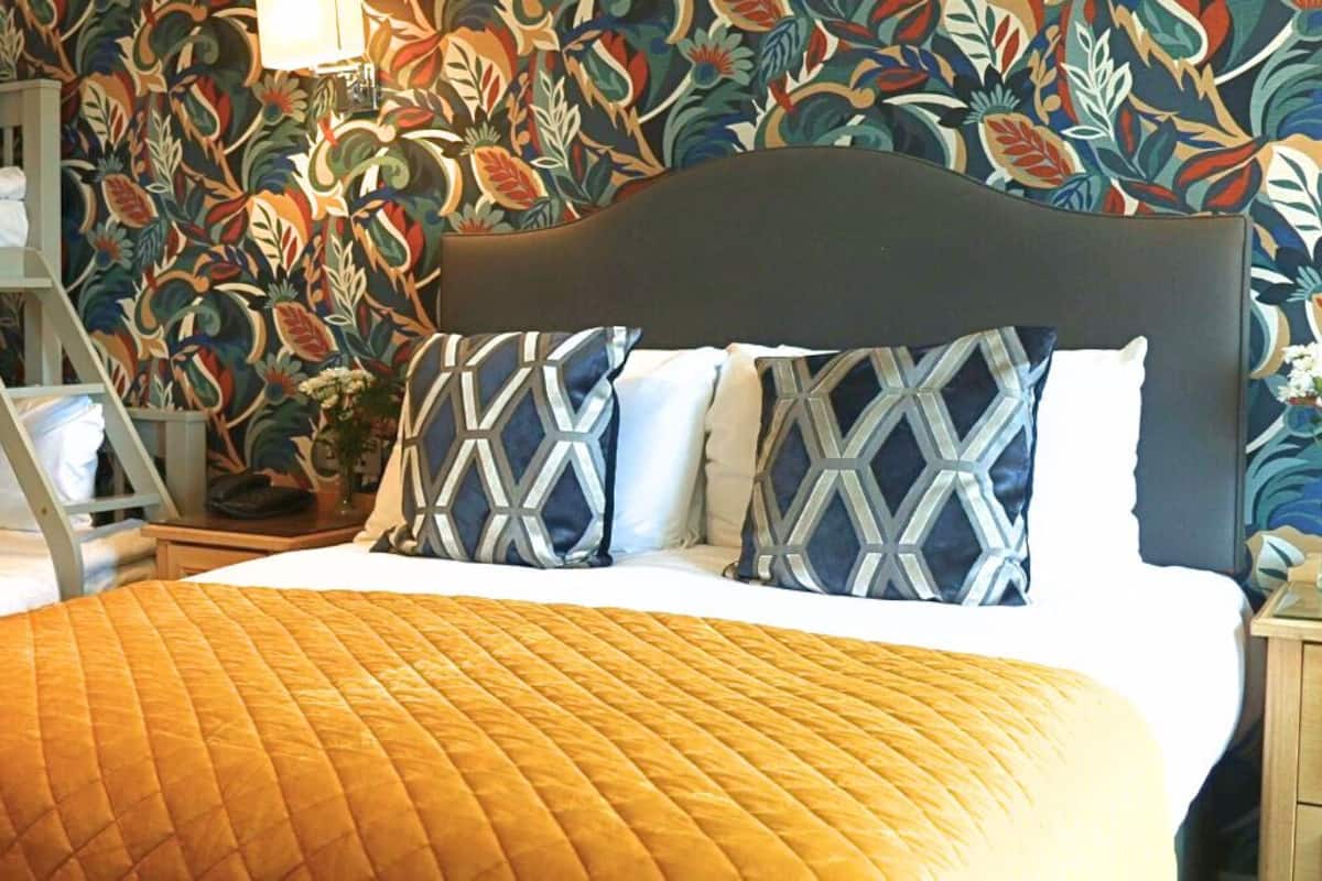 Quarto com duas camas, uma beliche, papel de parede floral e uma mesa de cabeceira com abajur.