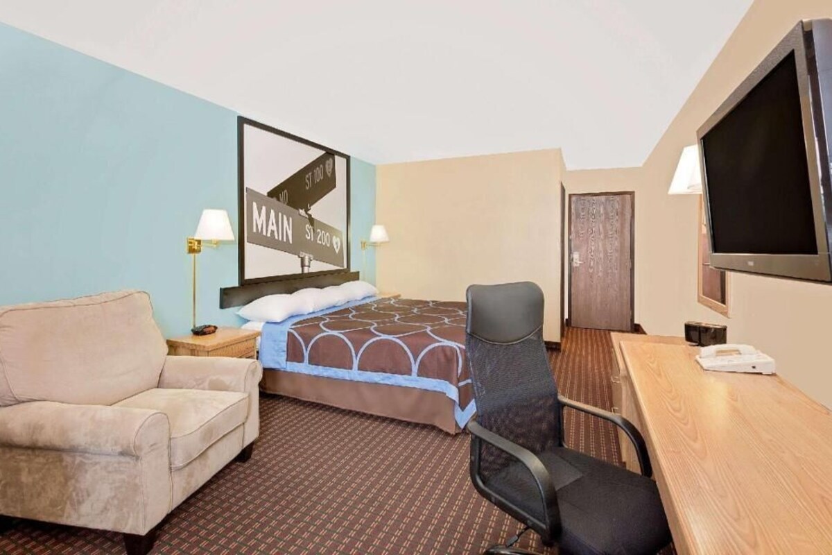 Quarto de hotel com cama, escrivaninha, cadeira, televisão e placa indicando o número do quarto.