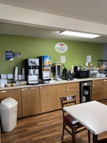 Espaço de café da manhã com máquina de café, dispensador de suco, torradeira e placa indicando café da manhã cortesia.