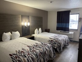 Quarto de hotel com duas camas, uma mesa de cabeceira, uma luminária na parede, uma janela com cortinas e um ar condicionado.