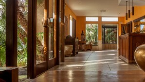 Um corredor com piso de madeira, grandes janelas e vista para plantas tropicais.