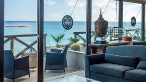 Uma sala de estar moderna com vista para o mar, com móveis de vime, uma mesa de centro de vidro e objetos decorativos.