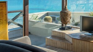 Uma sala de estar moderna com uma grande janela com vista para o oceano, uma mesa de centro de madeira e uma escultura de cacto.