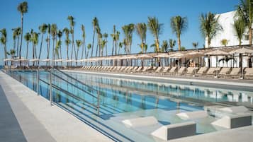 Uma área de piscina com espreguiçadeiras e guarda-sóis, rodeada por palmeiras.