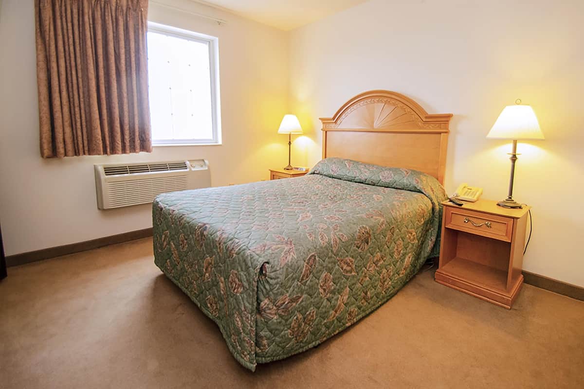 Quarto de hotel bem arrumado com uma cama grande, duas luminárias de cabeceira, mesa de cabeceira com telefone e uma janela com cortinas.