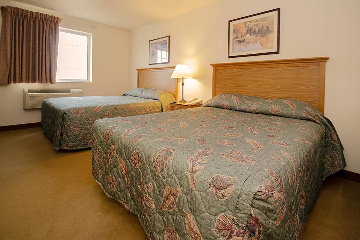 Quarto de hotel com duas camas, uma janela com cortinas, um quadro na parede e uma luminária na mesa de cabeceira.