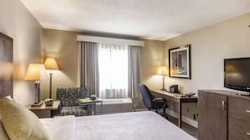 Quarto de hotel com cama, escrivaninha, cadeira, televisão e janela com cortinas.