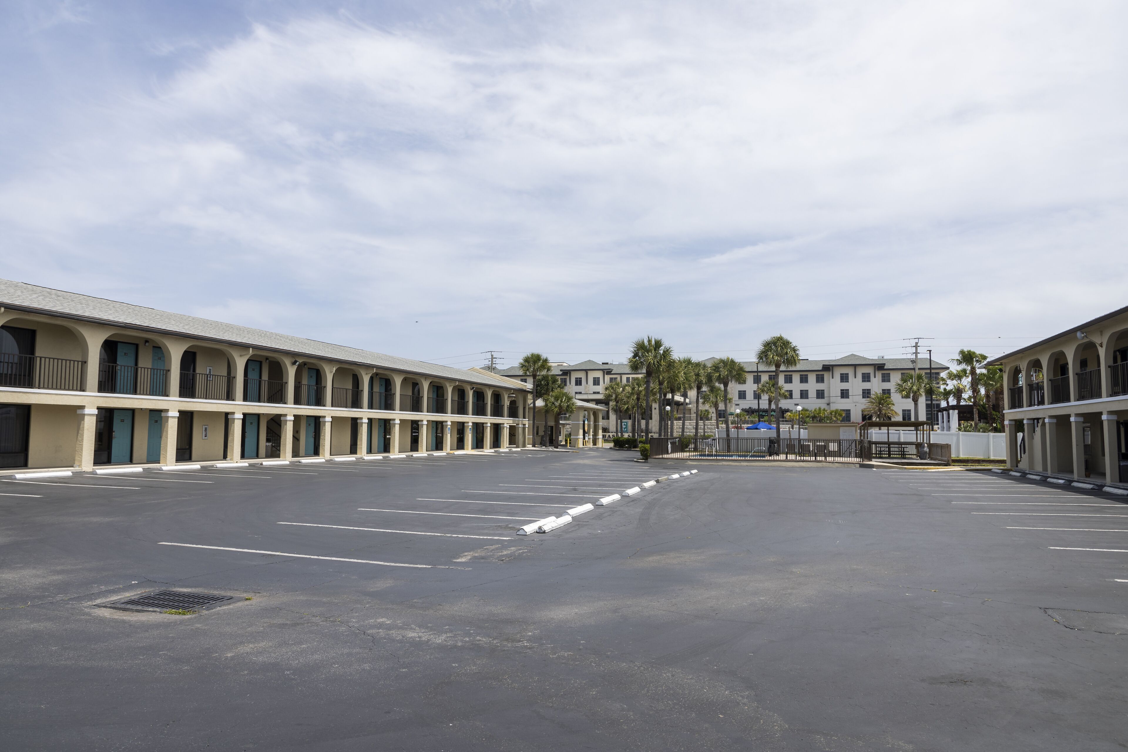 Um amplo estacionamento vazio com uma fileira de edifícios no estilo motel ao fundo.