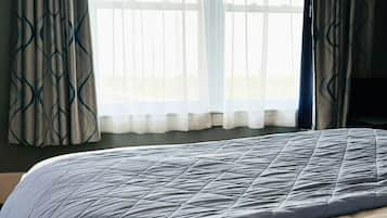 Uma cama com cobertura acolchoada, uma janela com cortinas leves e uma cortina estampada à esquerda.