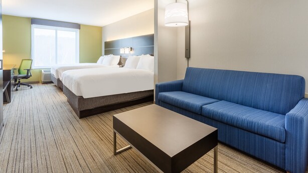Quarto de hotel com cama, sofá azul, mesa de centro, escrivaninha com cadeira e luminária.