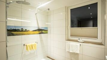 Uma casa de banho moderna com chuveiro, janela com persianas e um porta-toalhas.