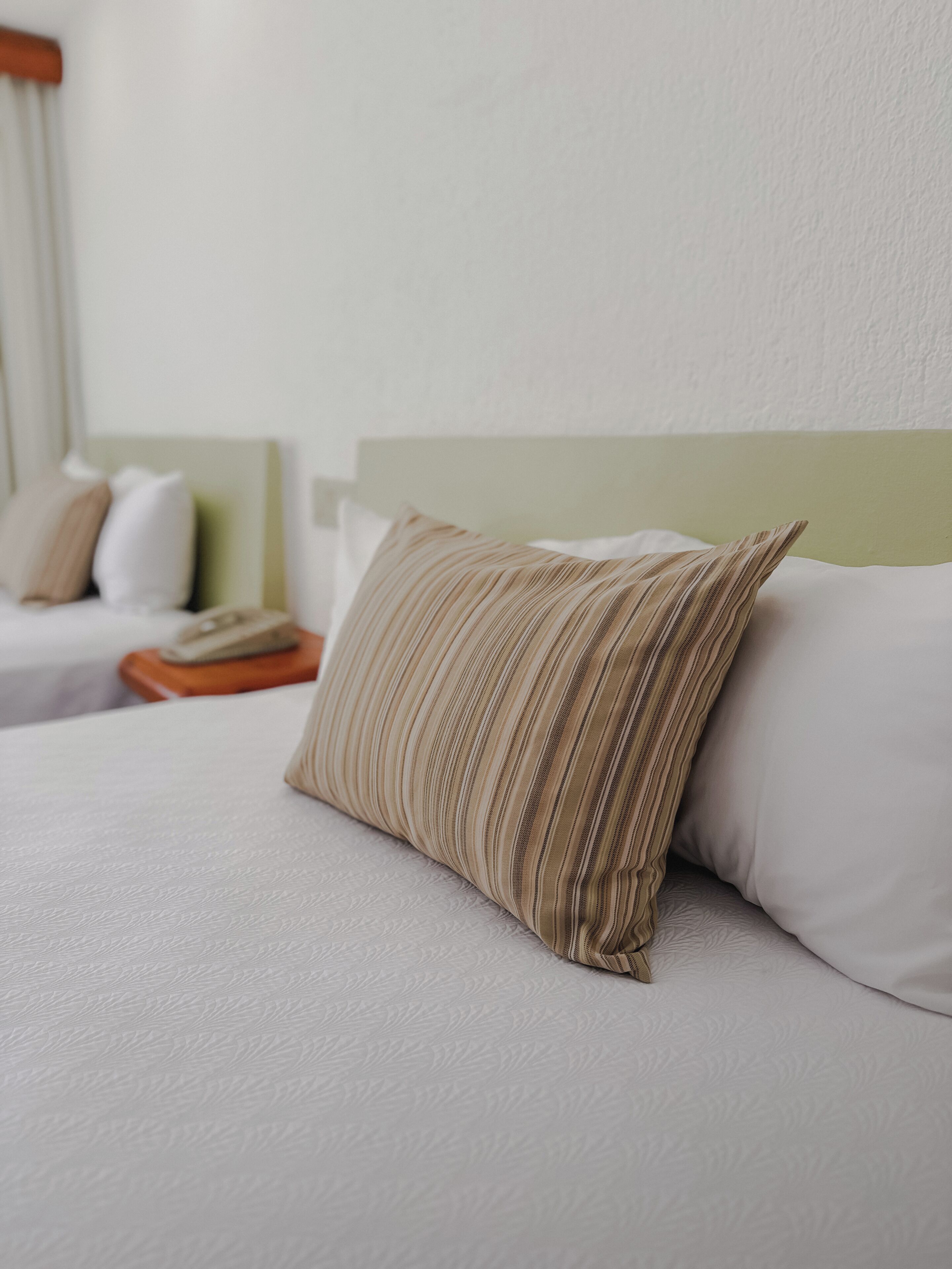 Cama bem arrumada com um travesseiro listrado e um travesseiro liso, uma mesa de cabeceira de madeira e um cabeceiro verde.