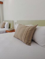 Cama bem arrumada com um travesseiro listrado e um travesseiro liso, uma mesa de cabeceira de madeira e um cabeceiro verde.