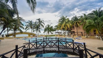 Uma área de piscina com deck de madeira, palmeiras e uma ponte.