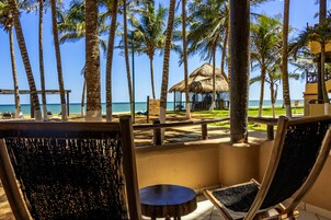 Vista da praia com palmeiras, uma cabana com telhado de palha e cadeiras de descanso.