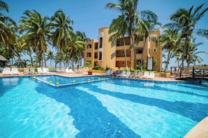 Piscina com espreguiçadeiras e palmeiras, cercada por um edifício com varandas.
