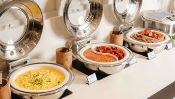 Buffet com pratos identificados, incluindo ovos mexidos, feijão assado, sopa de tomate e linguiça.