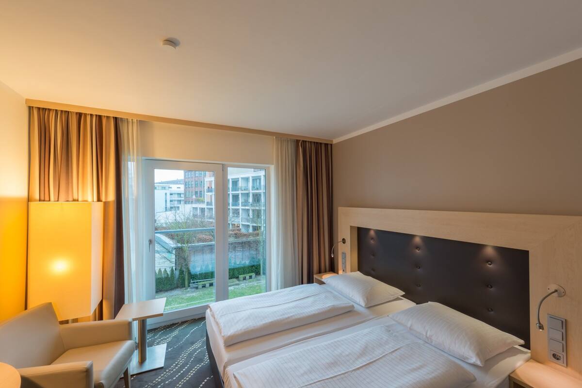 Quarto de hotel com duas camas, uma escrivaninha e vista para o exterior.