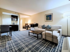 Quarto de hotel com cozinha compacta, sofá, mesa de centro e tapete estampado.
