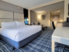 Quarto de hotel com uma cama grande, uma escrivaninha, um sofá e um tapete estampado.